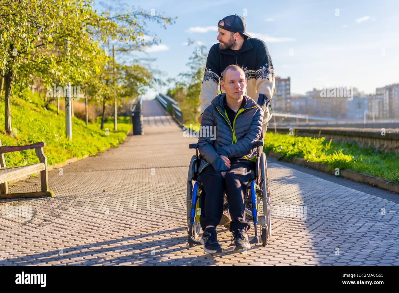 Smiling disabled person in a wheelchair walking with his brother in a ...