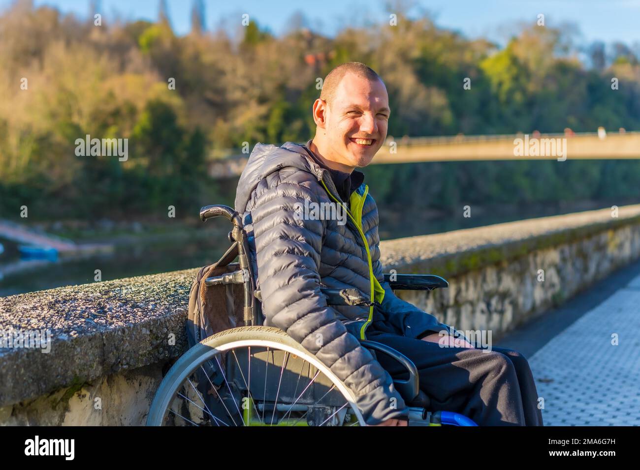 Portrait of a disabled person in a wheelchair smiling next to a river ...