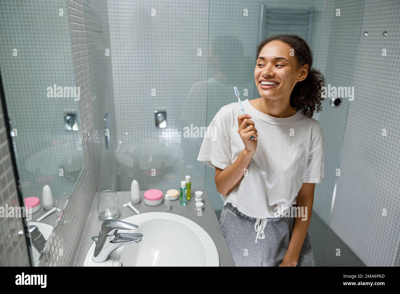 Smiling woman brushing teeth in front of her bathroom mirror. Morning ...