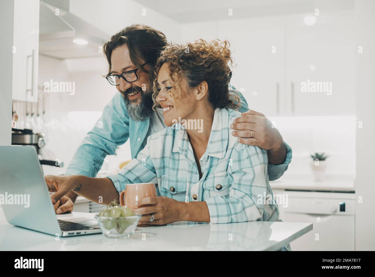 Happy husband and wife enjoying time in the kitchen using laptop ...