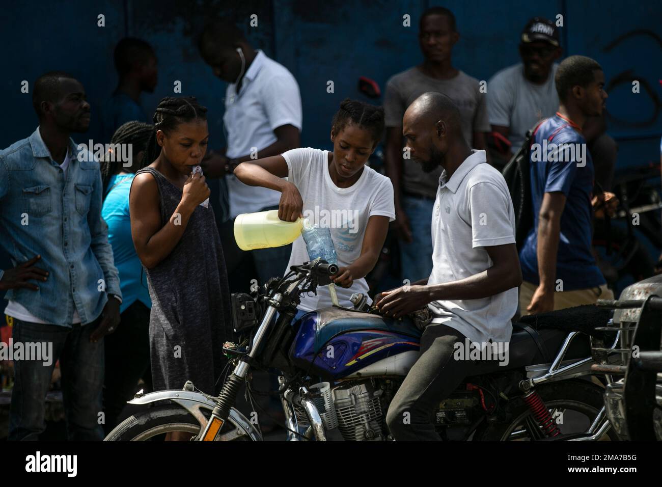 A woman sells gas to a motorcycle driver on a street in Port-au-Prince ...