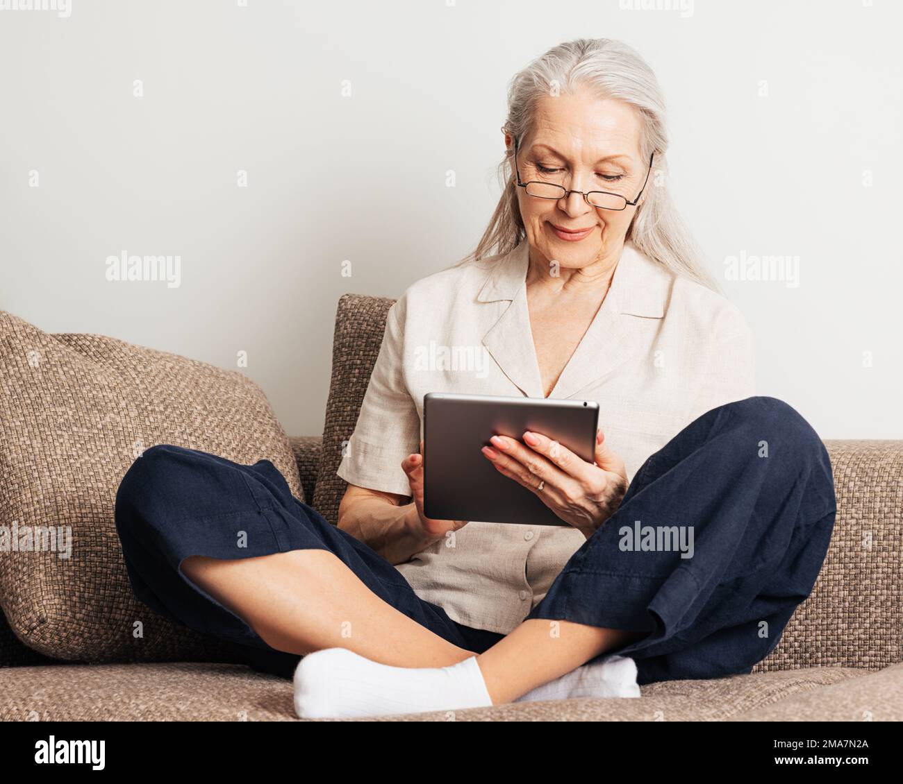 Senior woman with grey hair wearing glasses sitting with crossed legs ...
