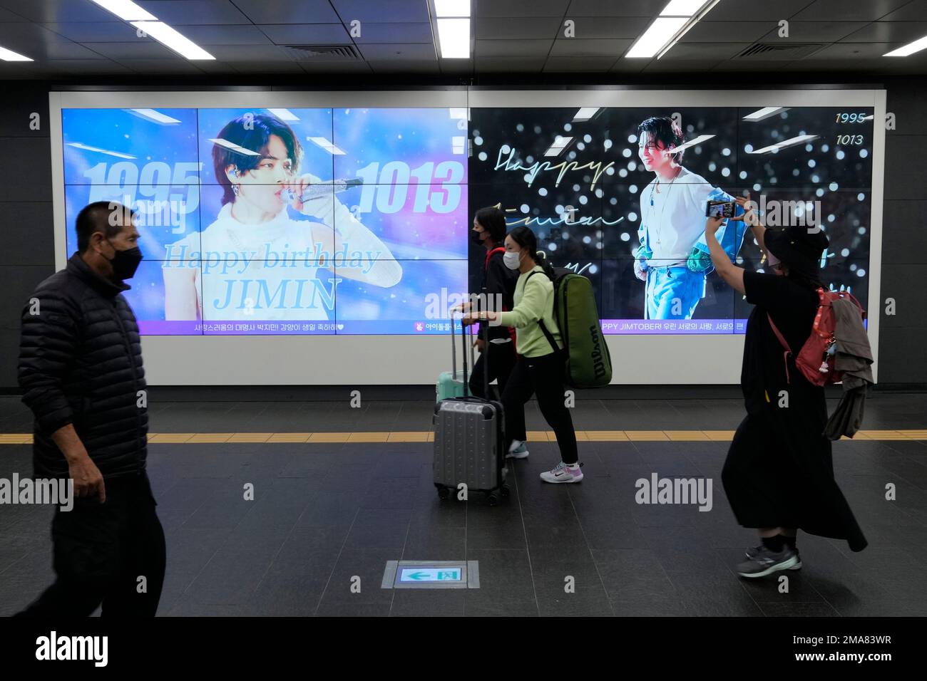 People pass by a screen installed to celebrate the birthday of Jimin, a ...