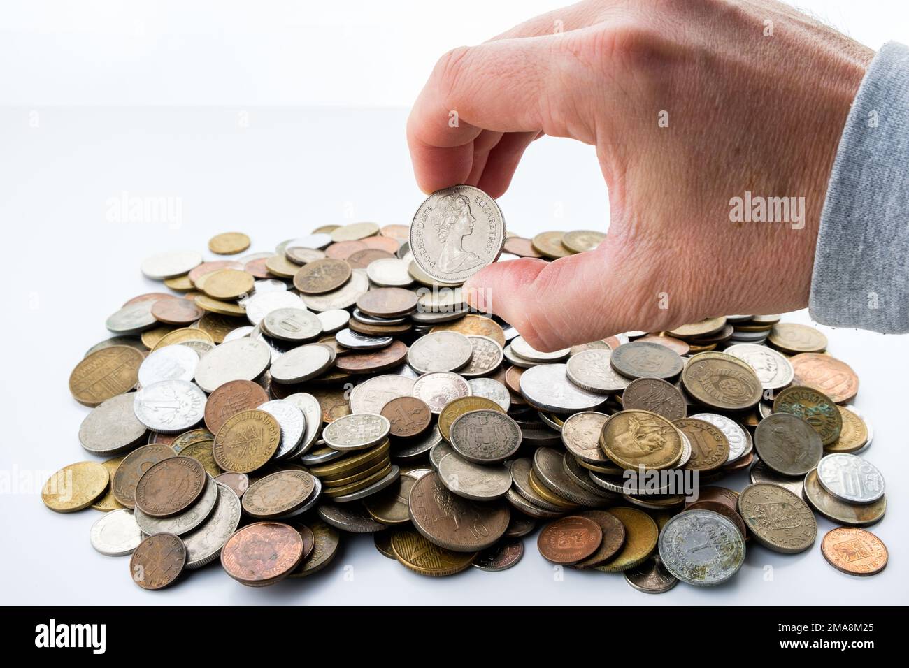 A hand holds a coin on a pile of old used coins. Current money of the ...