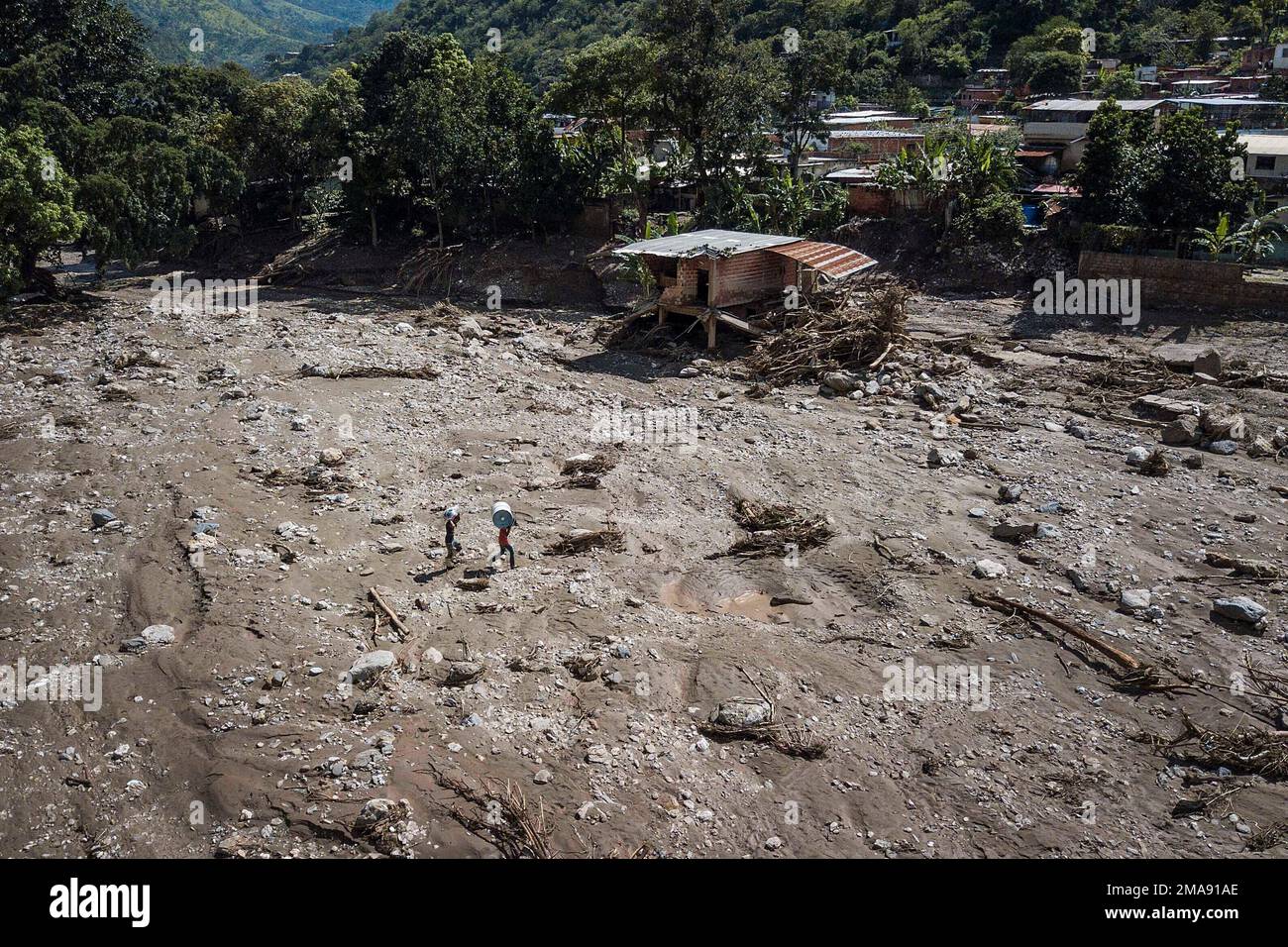 Men carry clothes and a barrel with water after a landslide and flood ...