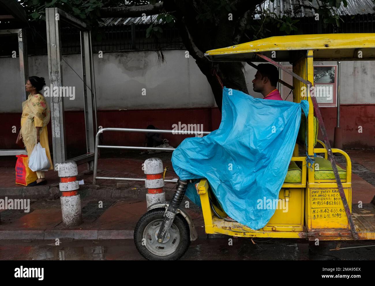 Driver of an electric passenger rickshaw covers himself with plastic to ...