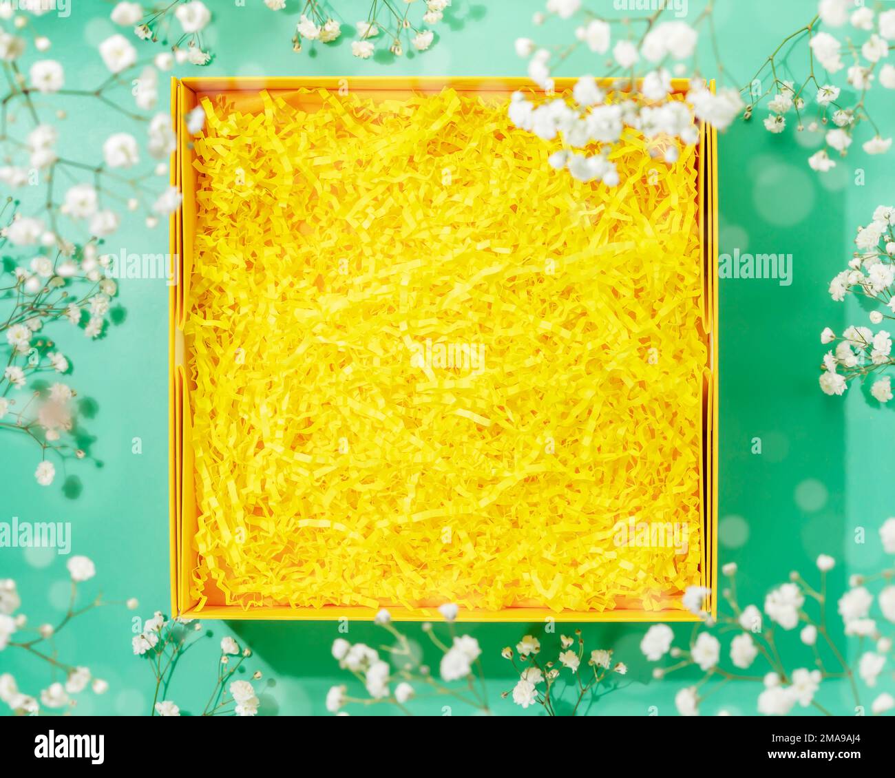 Opened gift box with shredded paper with white flowers. Yellow paper ...