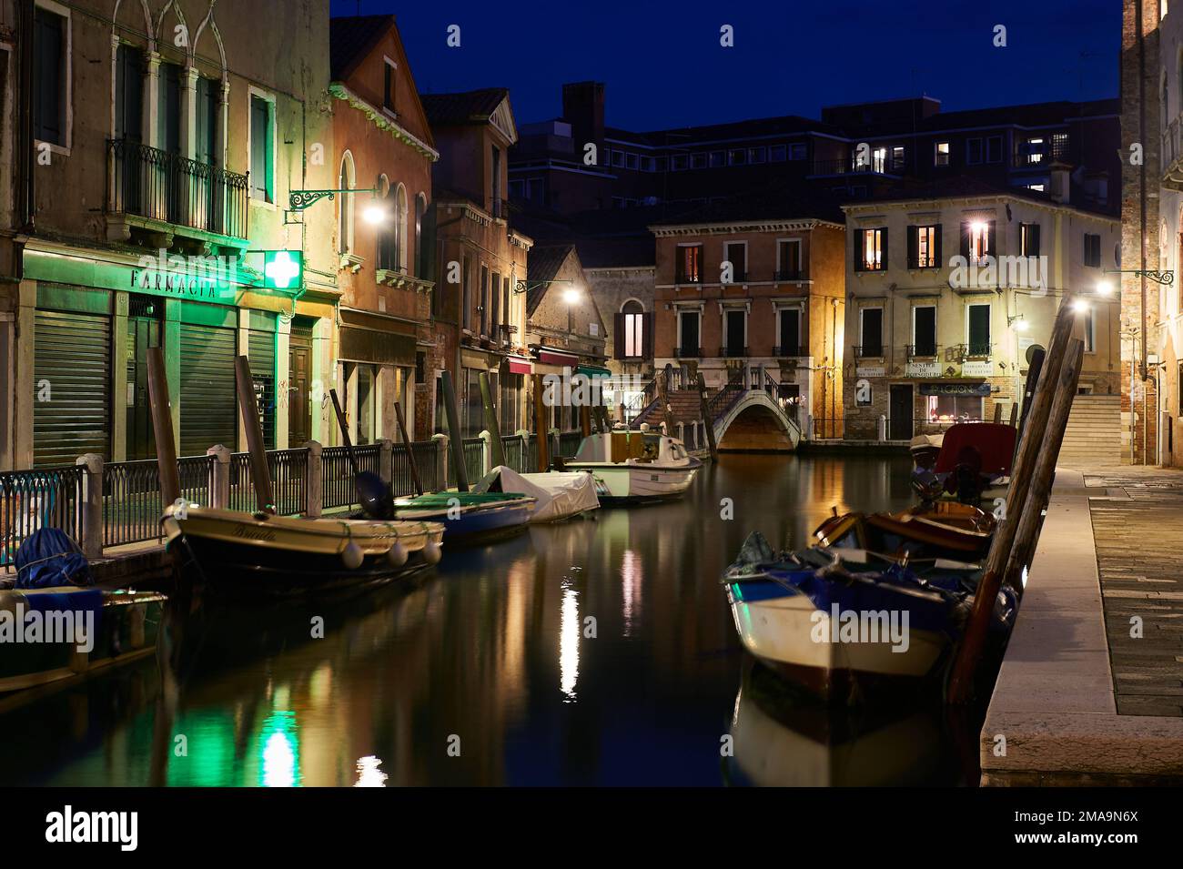 The city of Venice at night with little boats moored at the little ...