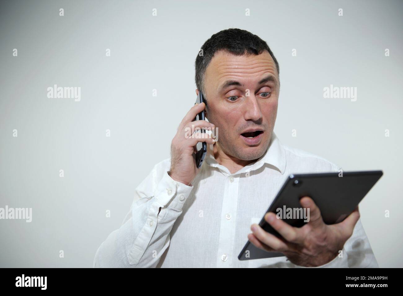 Surprised man in casual wear using digital tablet and making a face ...