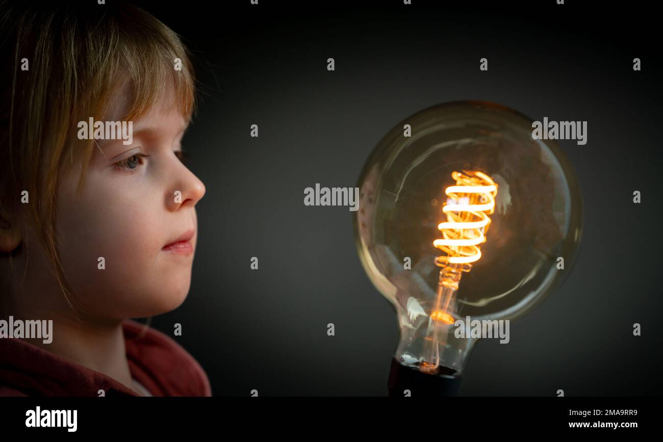 Young child looks focused to a huge filament light bulb. Symbol for a ...