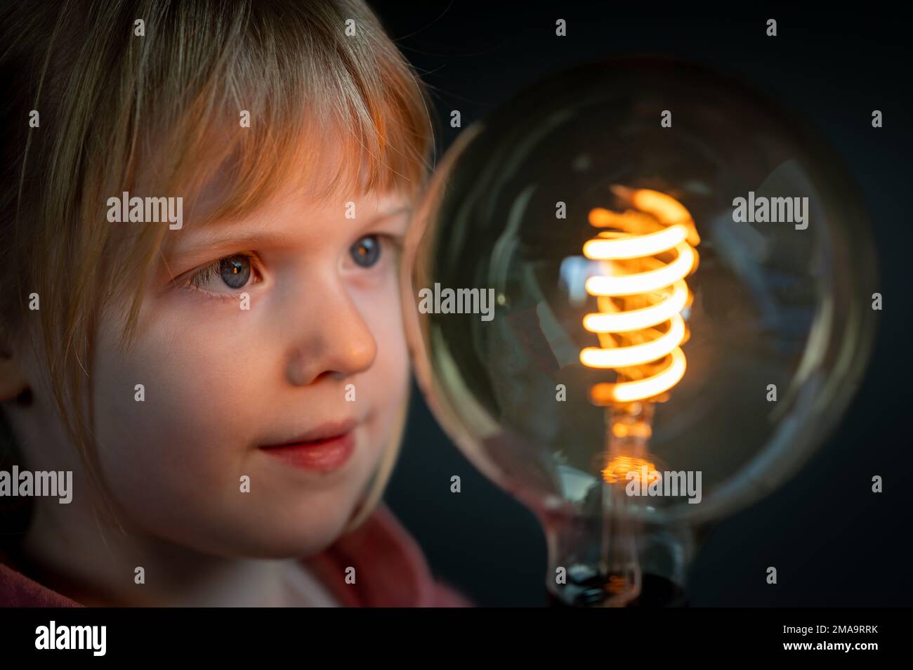 Young child looks focused to a huge filament light bulb. Symbol for a ...