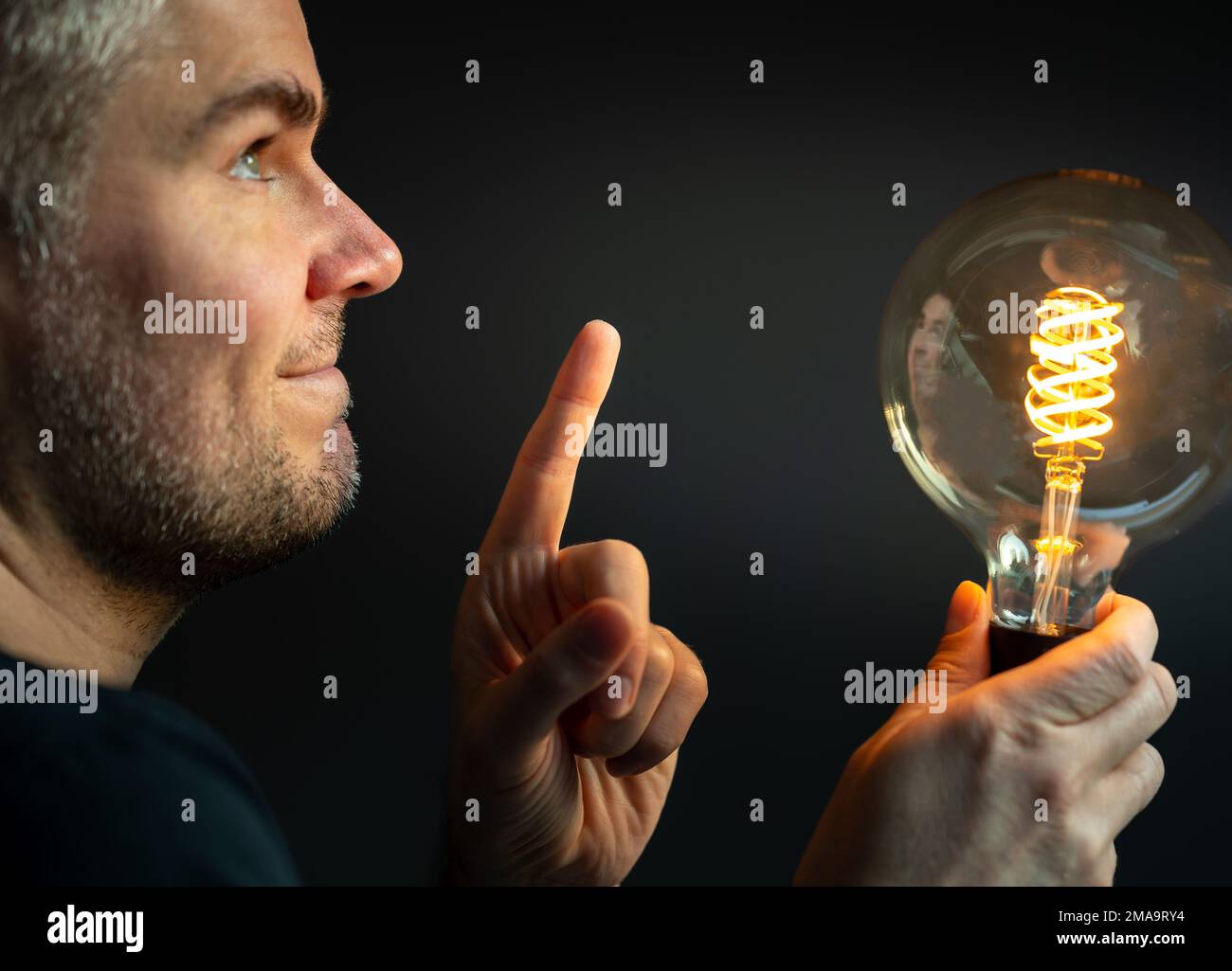 Symbol for saving energy. Man holds a filament light-bulb where the ...