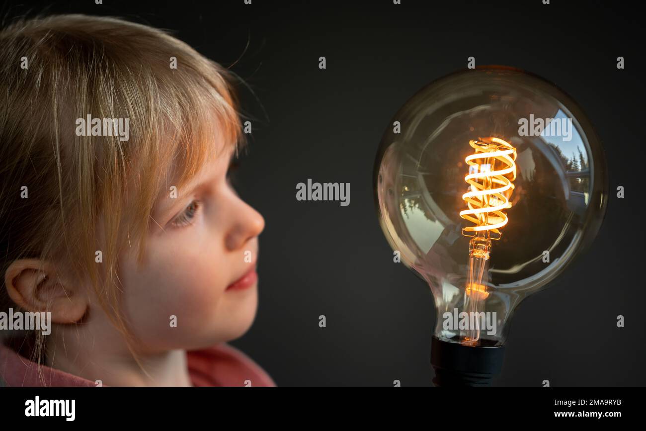 Young child looks curious to a huge filament light bulb. Symbol for a ...