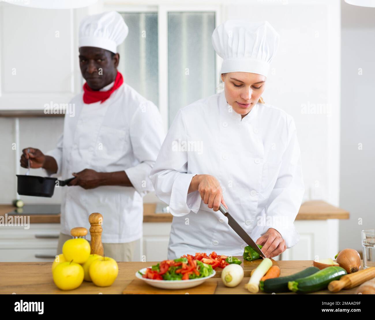 Young woman chef in white uniform working with male colleague in ...