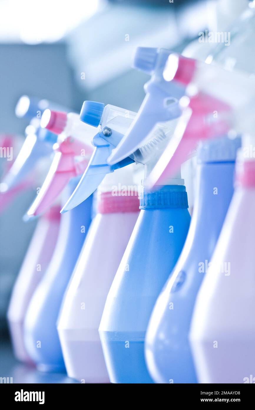 A vertical shot of pink and blue plastic spray bottles on a shelf in a ...
