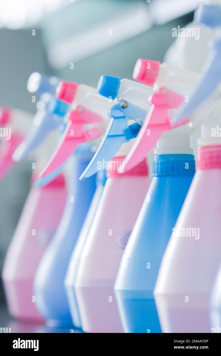 A vertical shot of pink and blue plastic spray bottles on a shelf in a ...