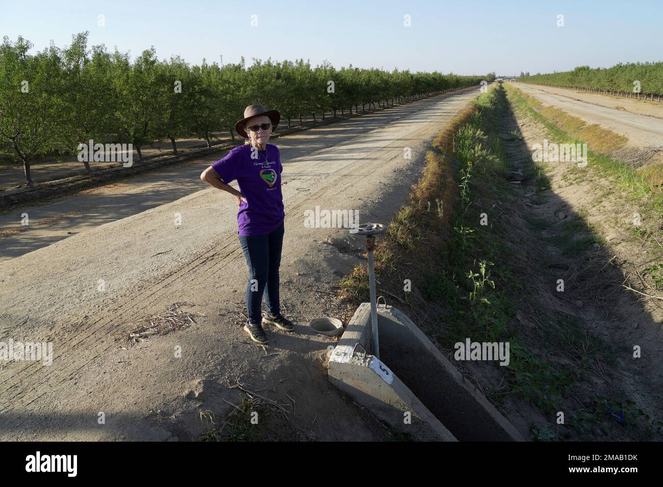 Elaine Moore stands next to a dry irrigation canal and almond orchard ...