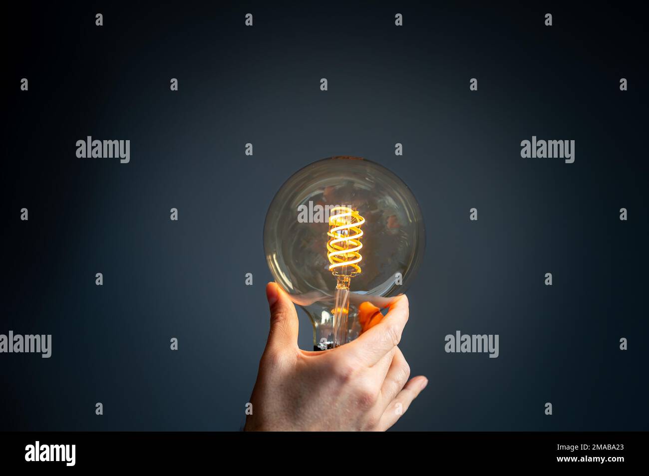 Symbol for saving energy. Hand holds a filament light-bulb where the ...