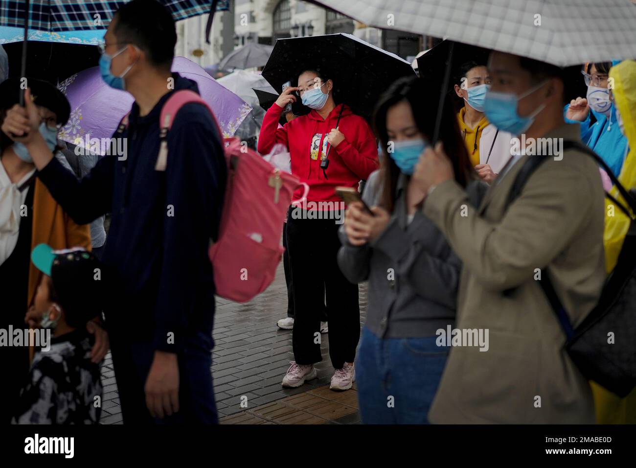 Visitors wearing face masks and holding umbrellas wait to cross a ...