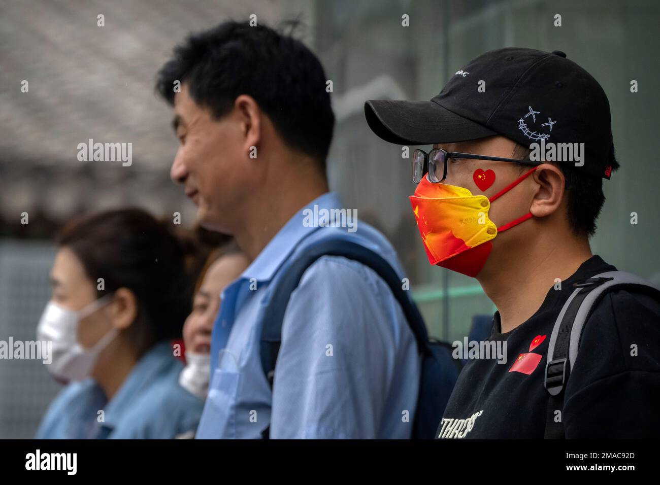 A man wearing a face mask and a sticker with the Chinese flag stands ...
