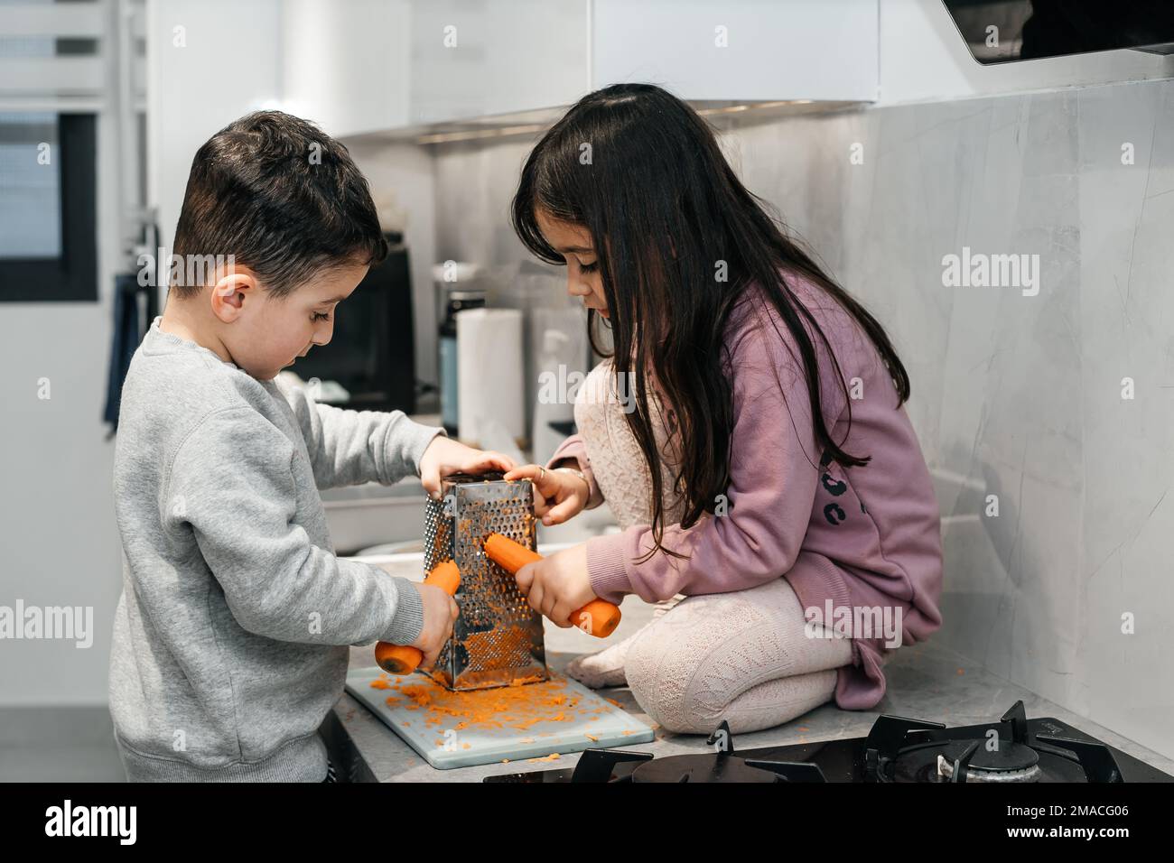 Brother and sister cook in the kitchen together, grating carrots ...