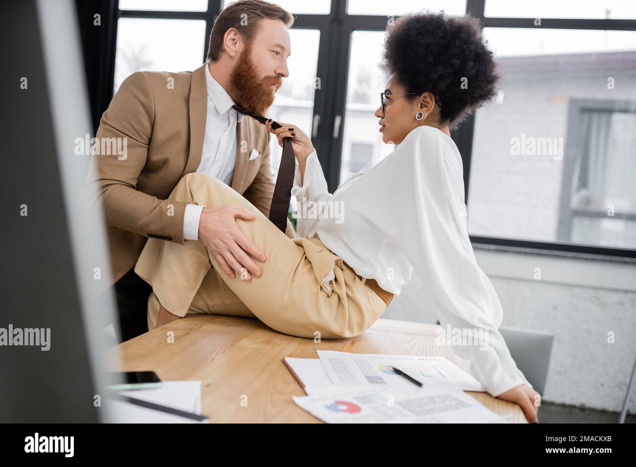 Side View Of African American Woman Pulling Tie Of Bearded Man Sitting