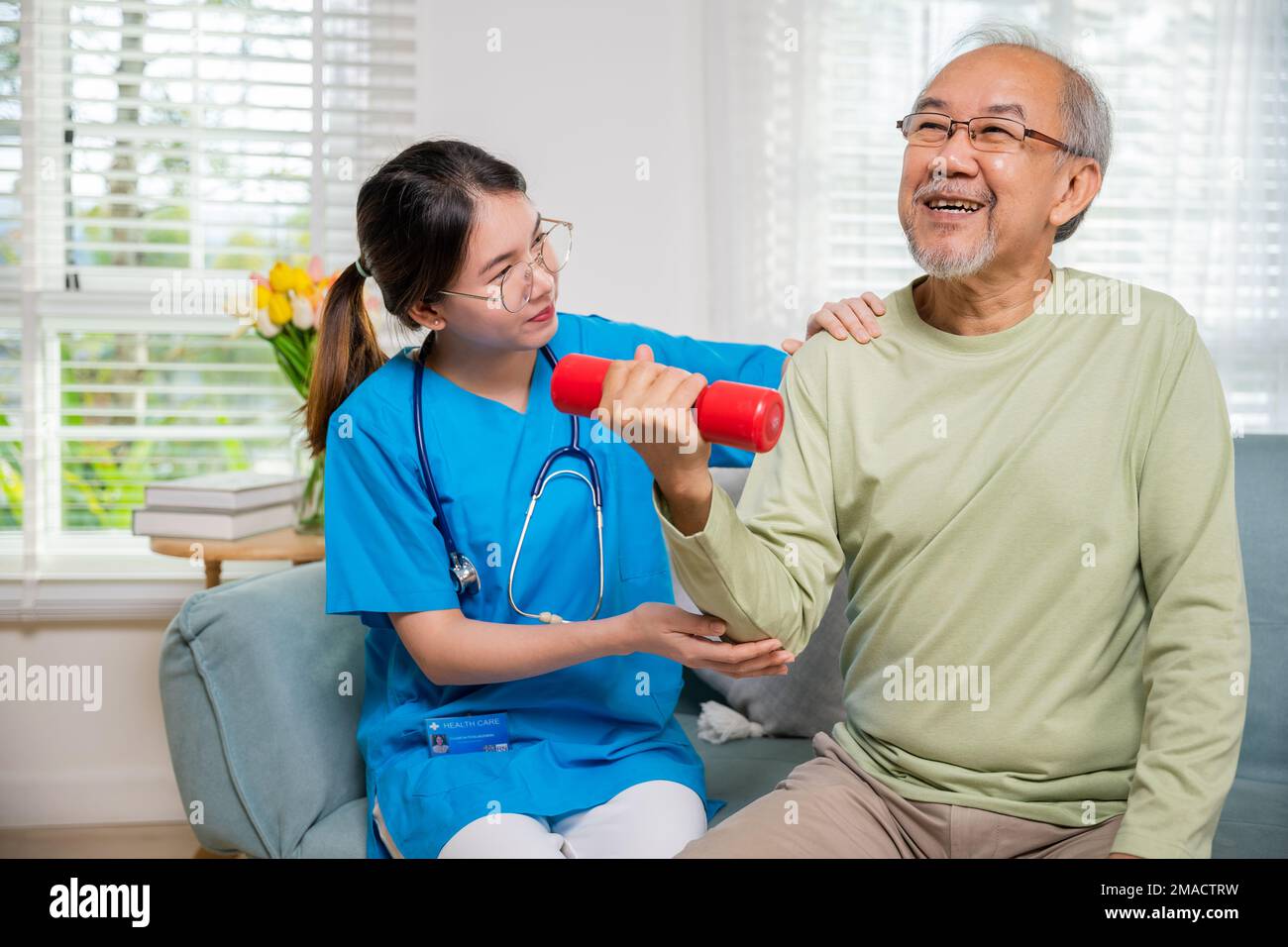 Asian nurse physiotherapist helping senior man in lifting dumbell at retirement home Stock Photo ...