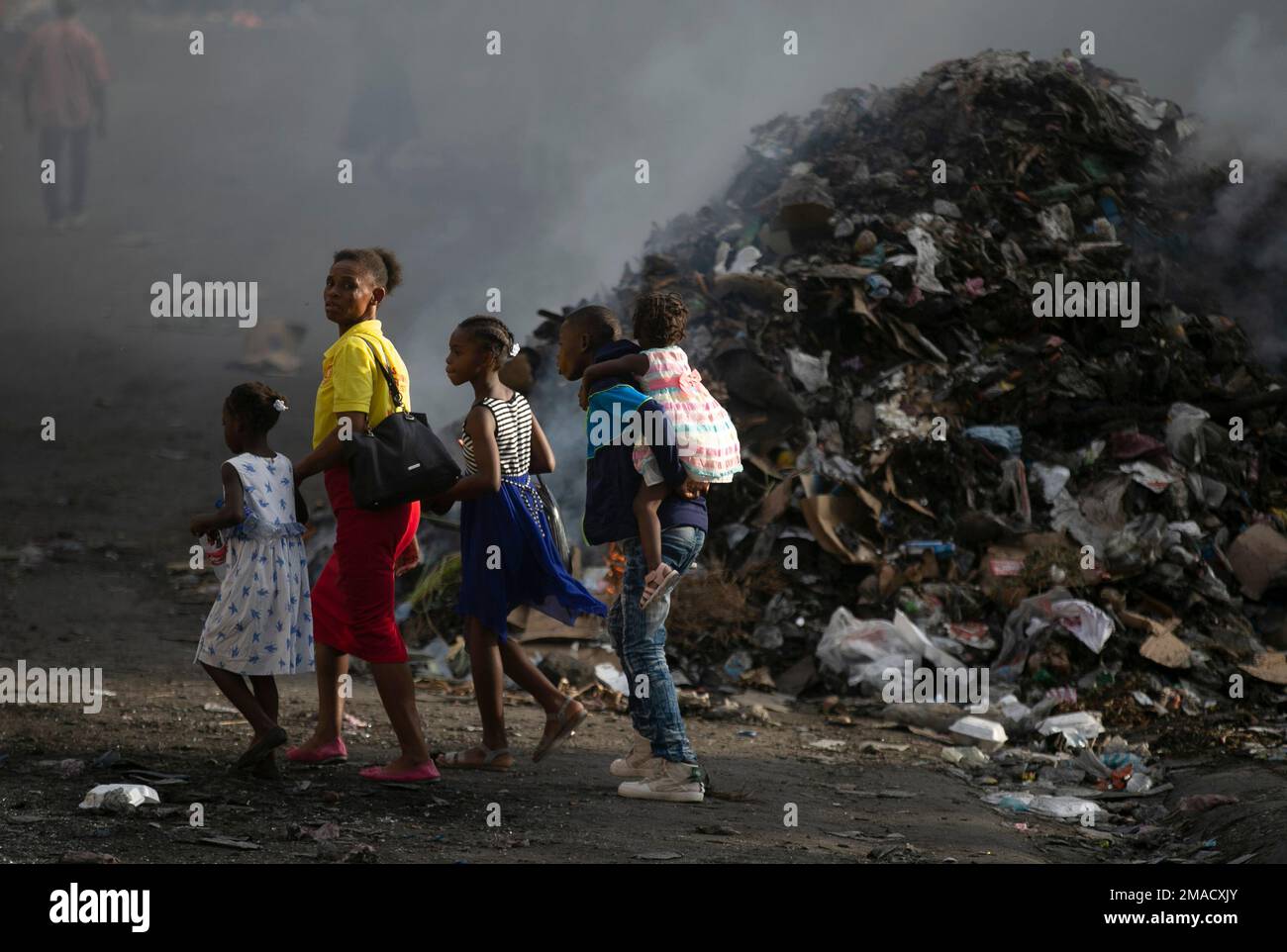 A woman with her children walks next to a smoldering pile of garbage in ...