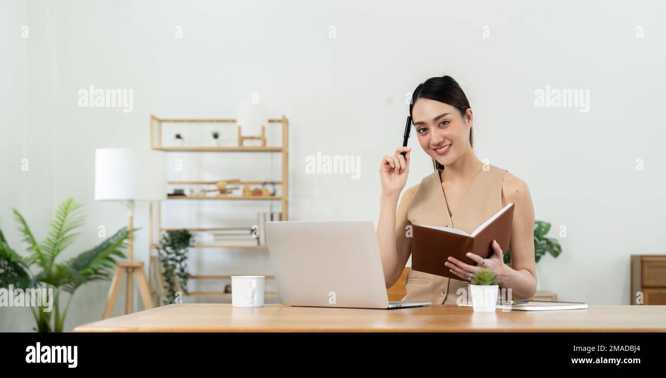 Happy Asian woman using laptop while taking note at home Stock Photo ...