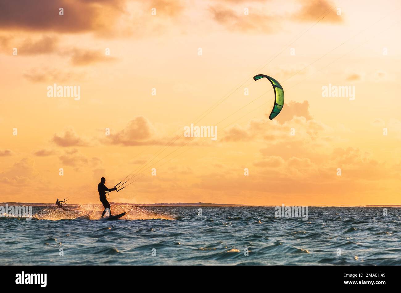 Sunset sky over the Indian Ocean bay with a two kiteboarders riding ...