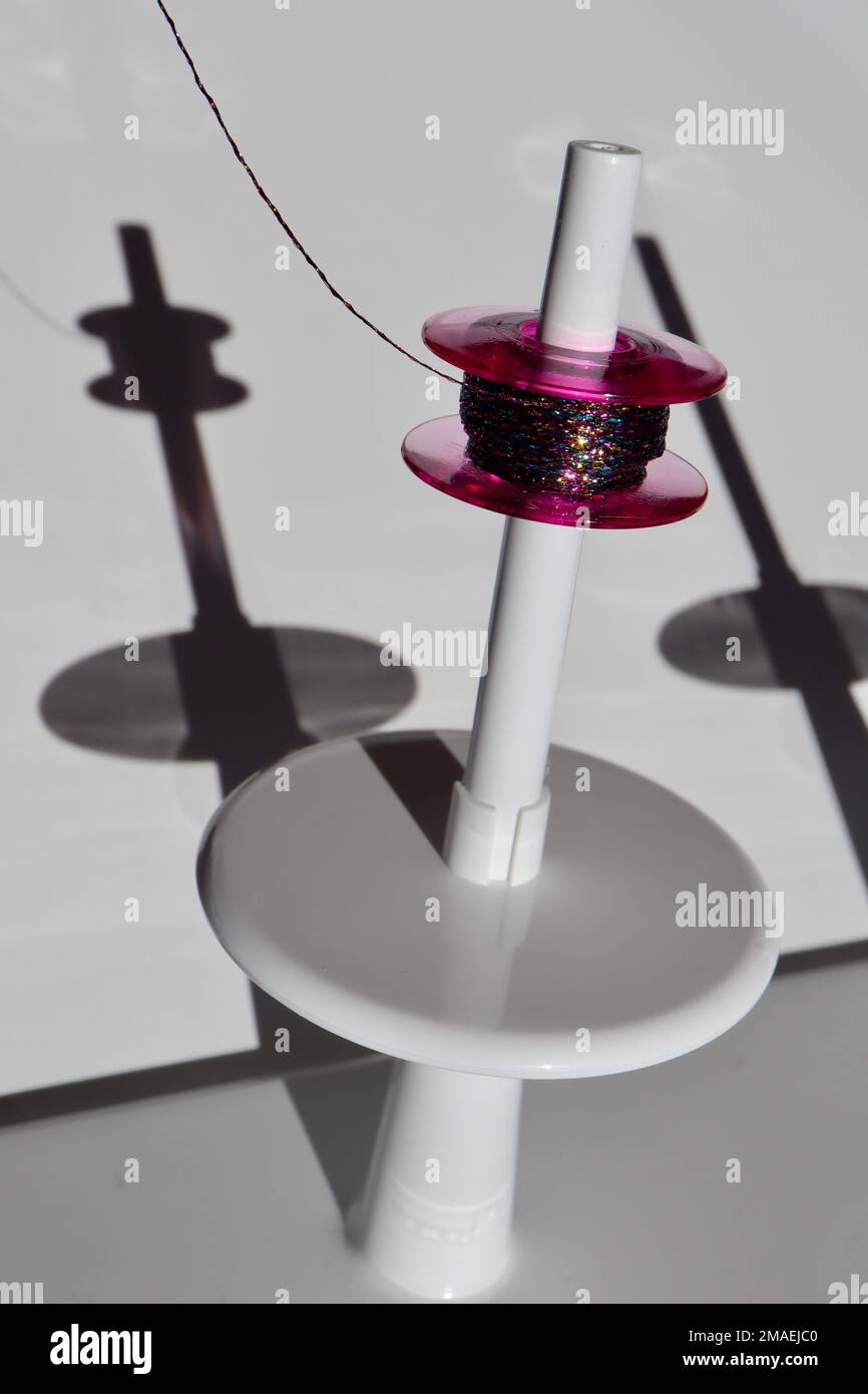 Macro of rainbow-coloured metallic yarn on a semi-transparent deep pink ...