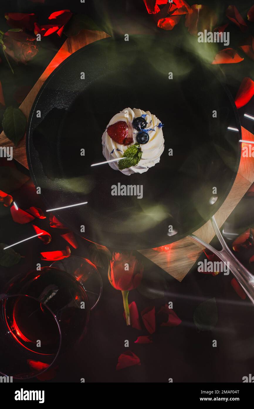 black frying pan with a pavlova cake and scattered red rose petals on a ...