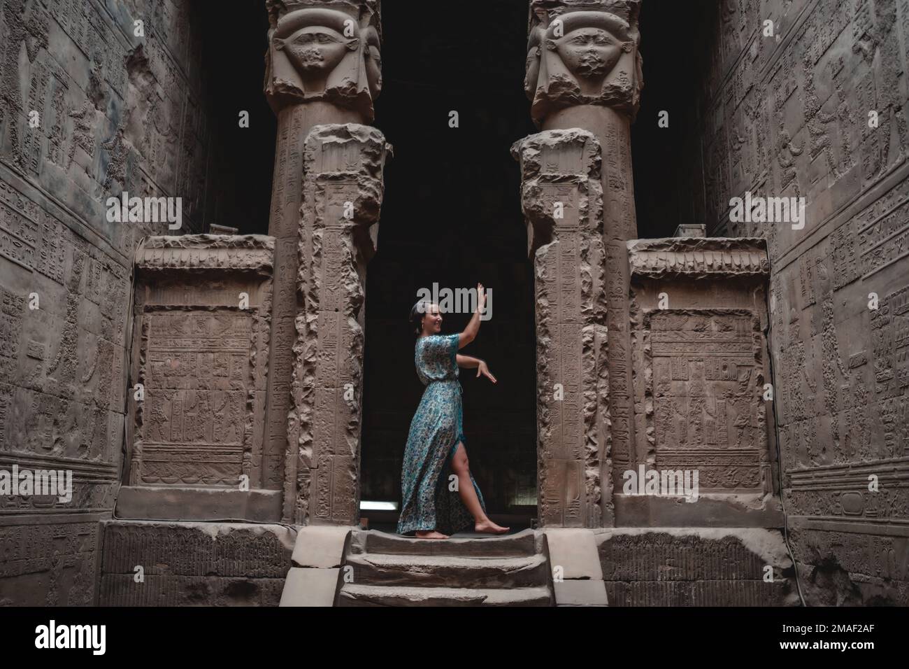 A beautiful woman in a blue dress dancing between the ancient columns ...