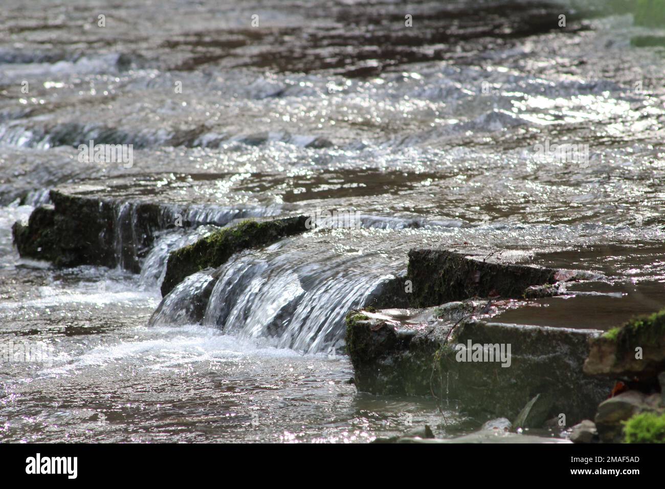A selective focus of a water flowing over a stone cascade, with a ...
