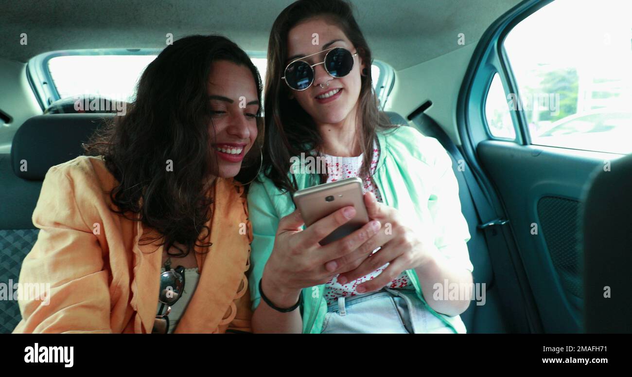 Authentic friends laughing together while sharing content on smartphone ...