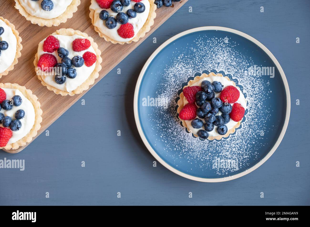 Raspberry and blueberry vanilla custard tarts on a blue table Stock ...