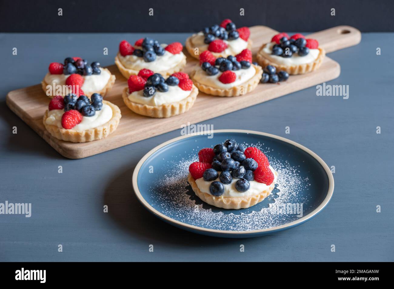 Raspberry and blueberry tarts on a blue table against a grey background ...