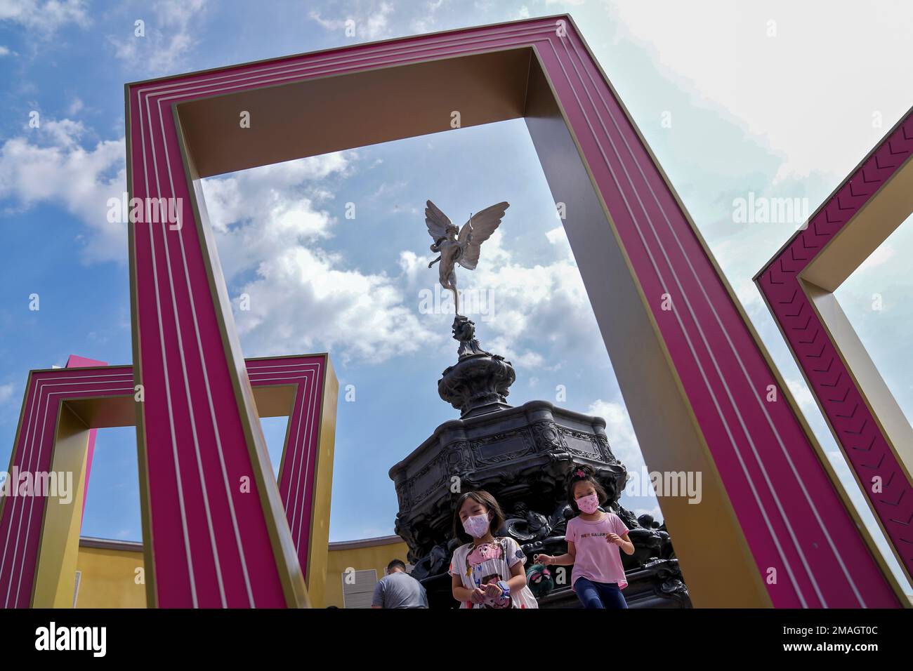Children wearing face masks play at a frame shaped art installation ...