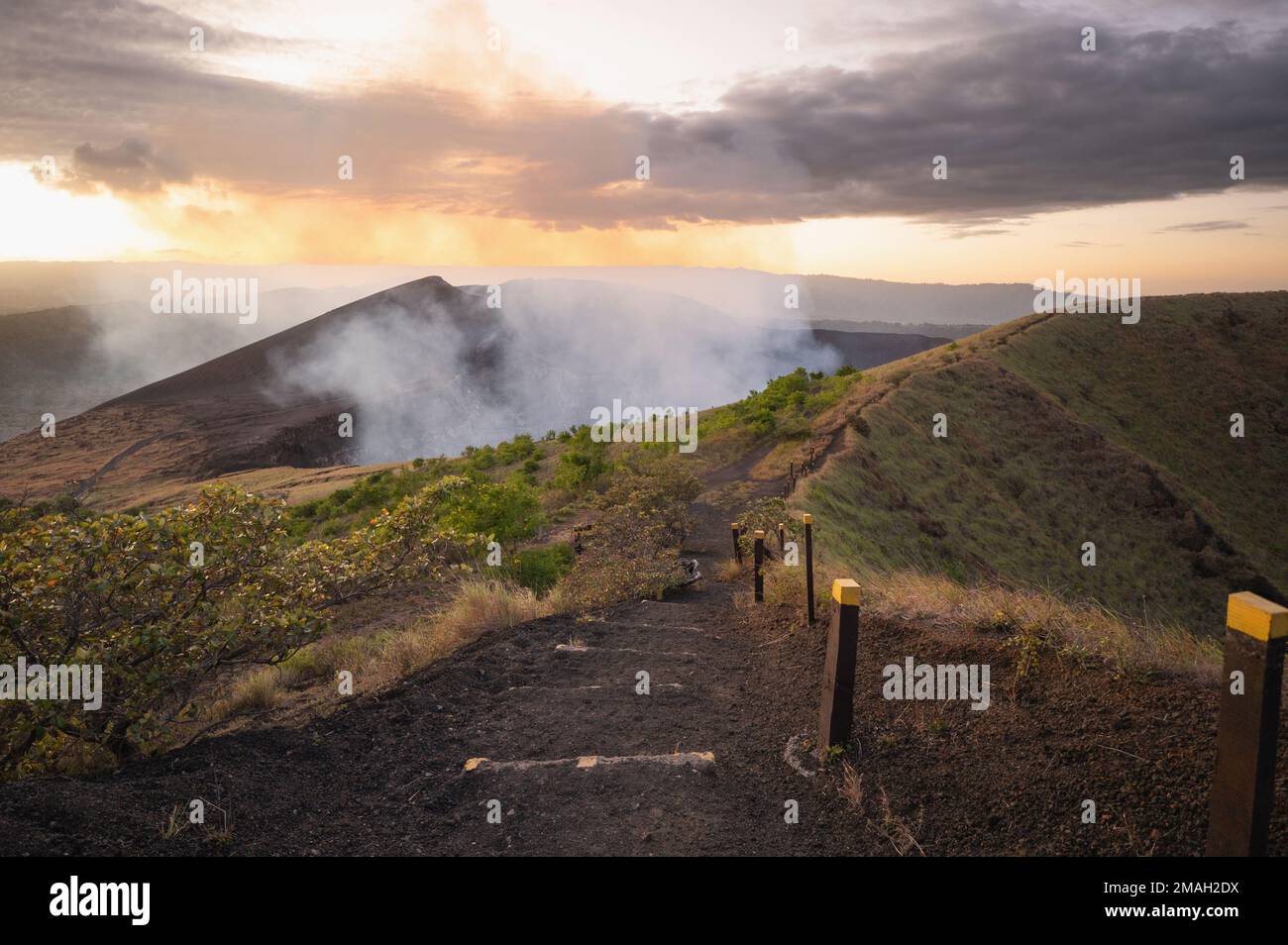 Hiking path in volcano crater with smoke going up on sunset light time ...