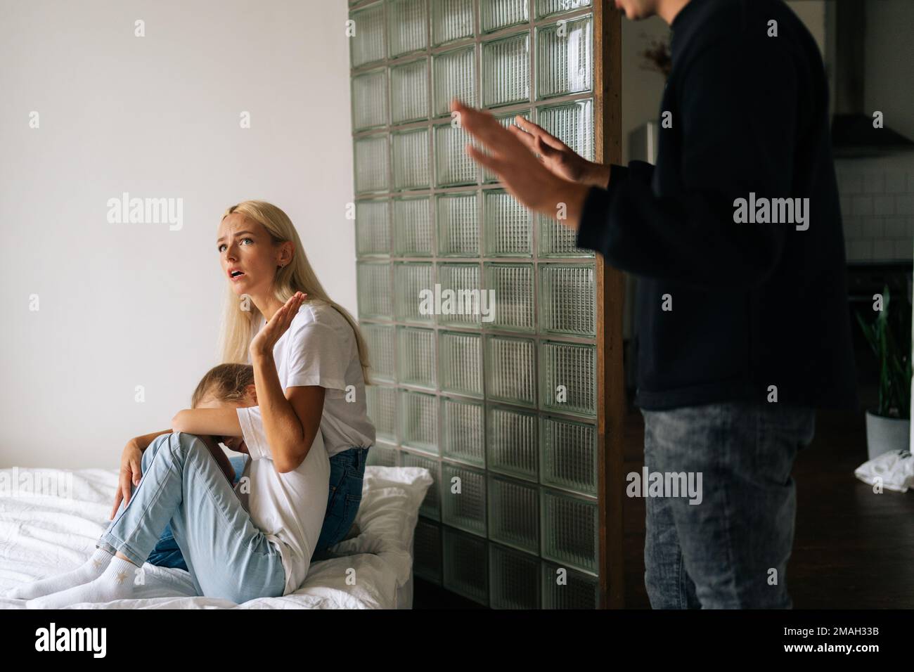 Cropped shot of scared mother and daughter hugging each other sitting on sofa while aggressive ...