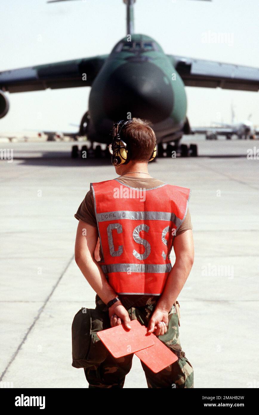 A ground crew member stands ready to signal the pilot of a C-5A Galaxy ...