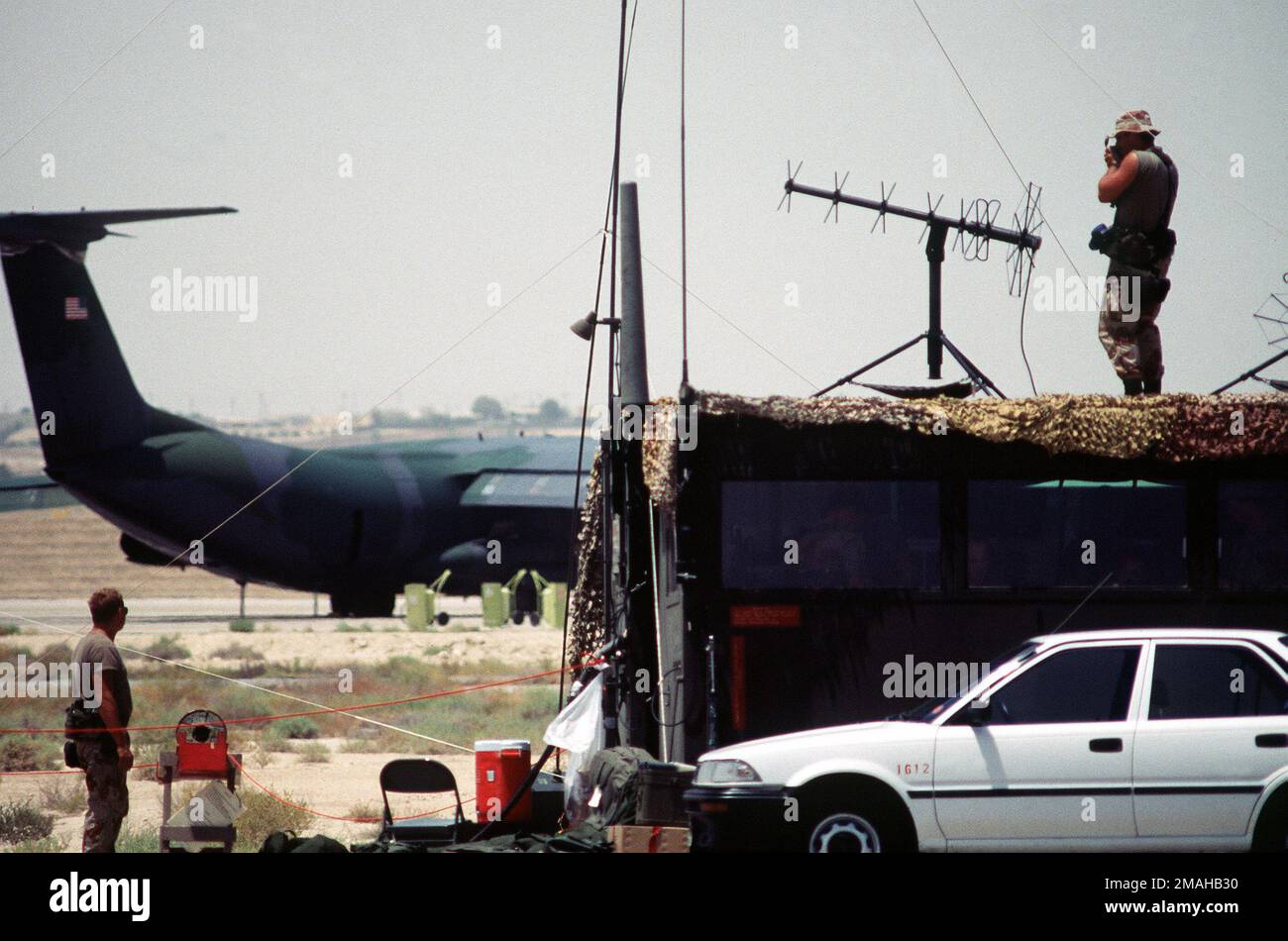 A soldier atop a camouflaged building photographs a Military Airlift ...