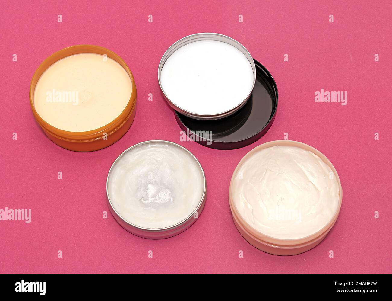 Open containers with beauty cream products isolated on pink background ...