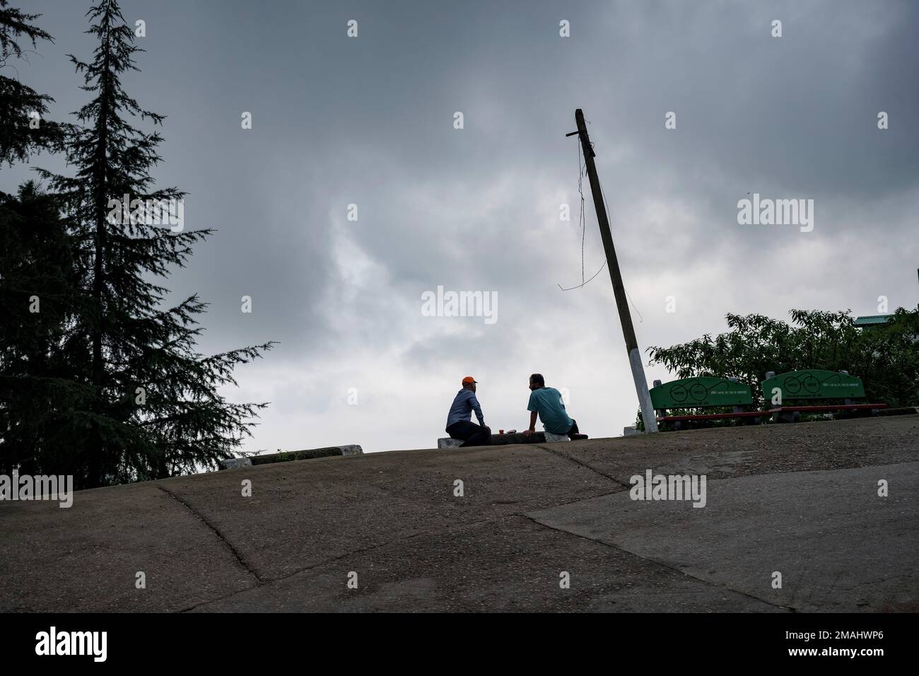 People sit by the side of a road eating snacks as rain clouds gather in ...