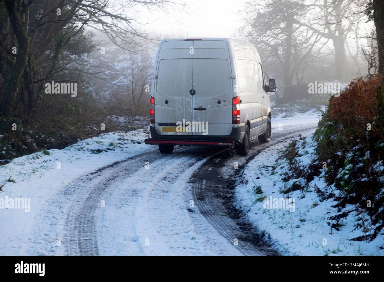 White van driving on ice and frozen snow on icy rural road country lane ...