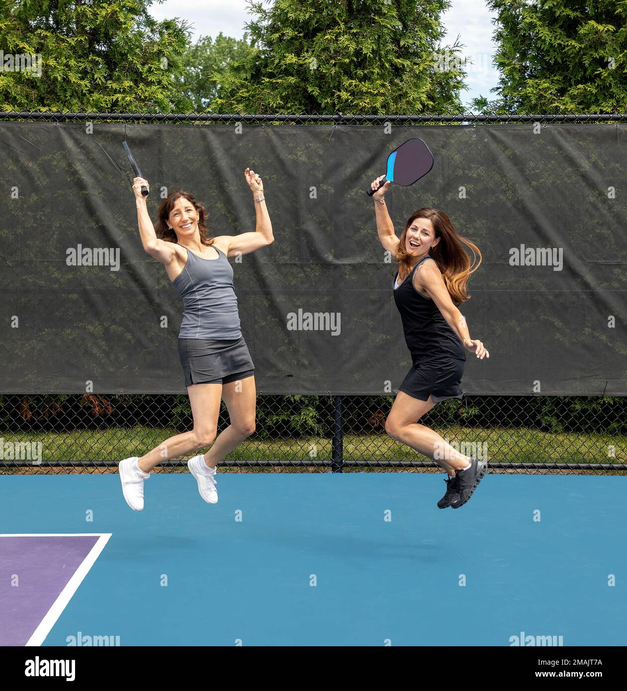 Two pickleball players jumping with paddles on a court during summer ...