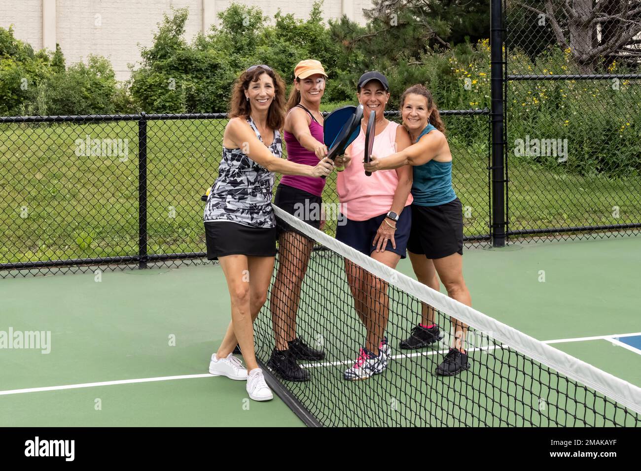 Four female pickleball players touch paddles after a competitive game ...