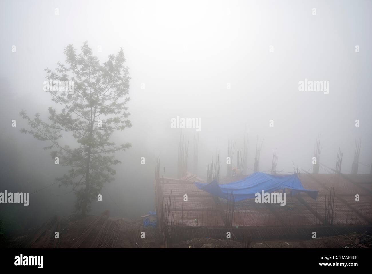 A construction crew works on the roof of a building under a thick fog ...