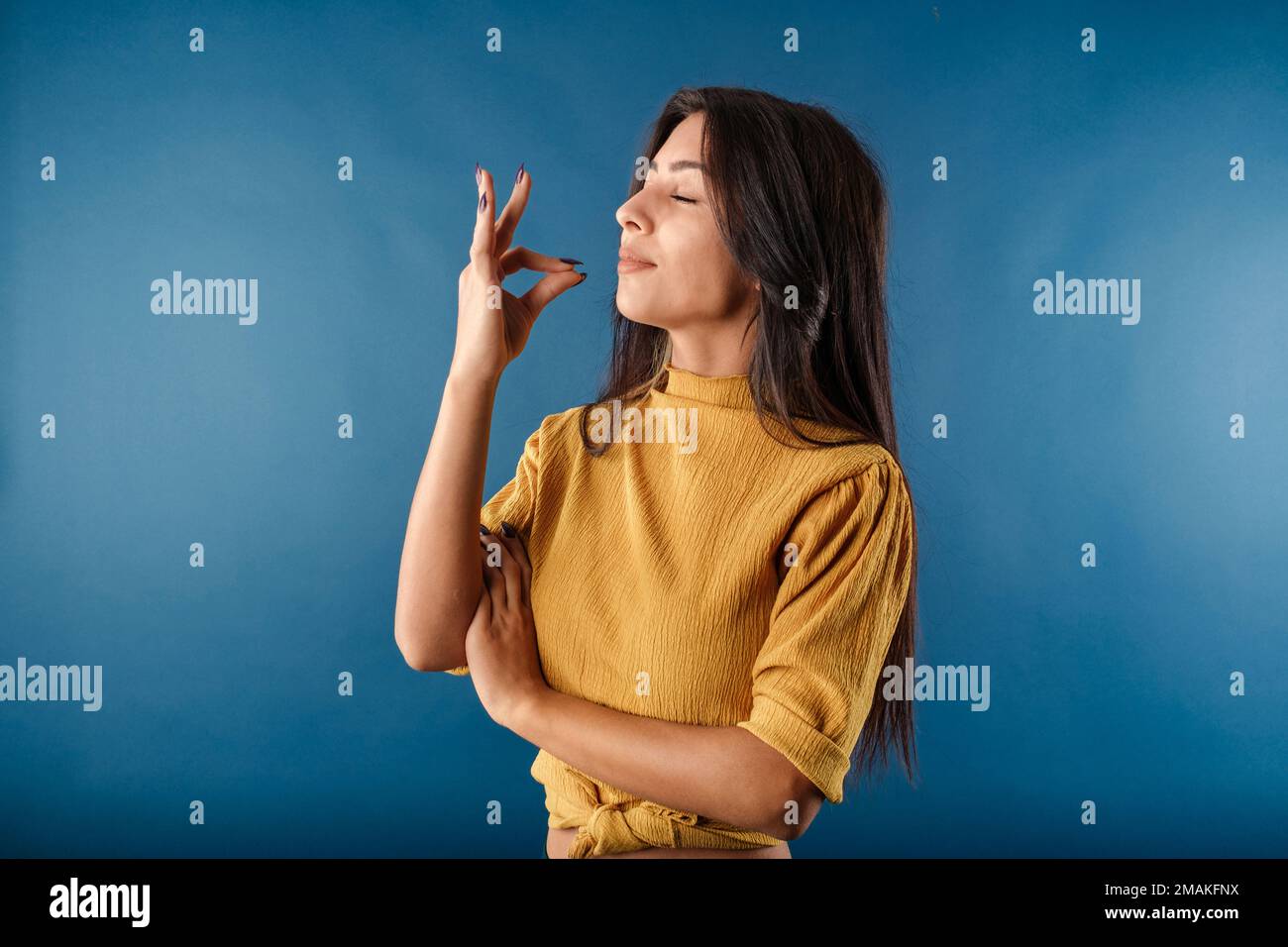 Young dark-haired woman wearing yellow top isolated over blue ...