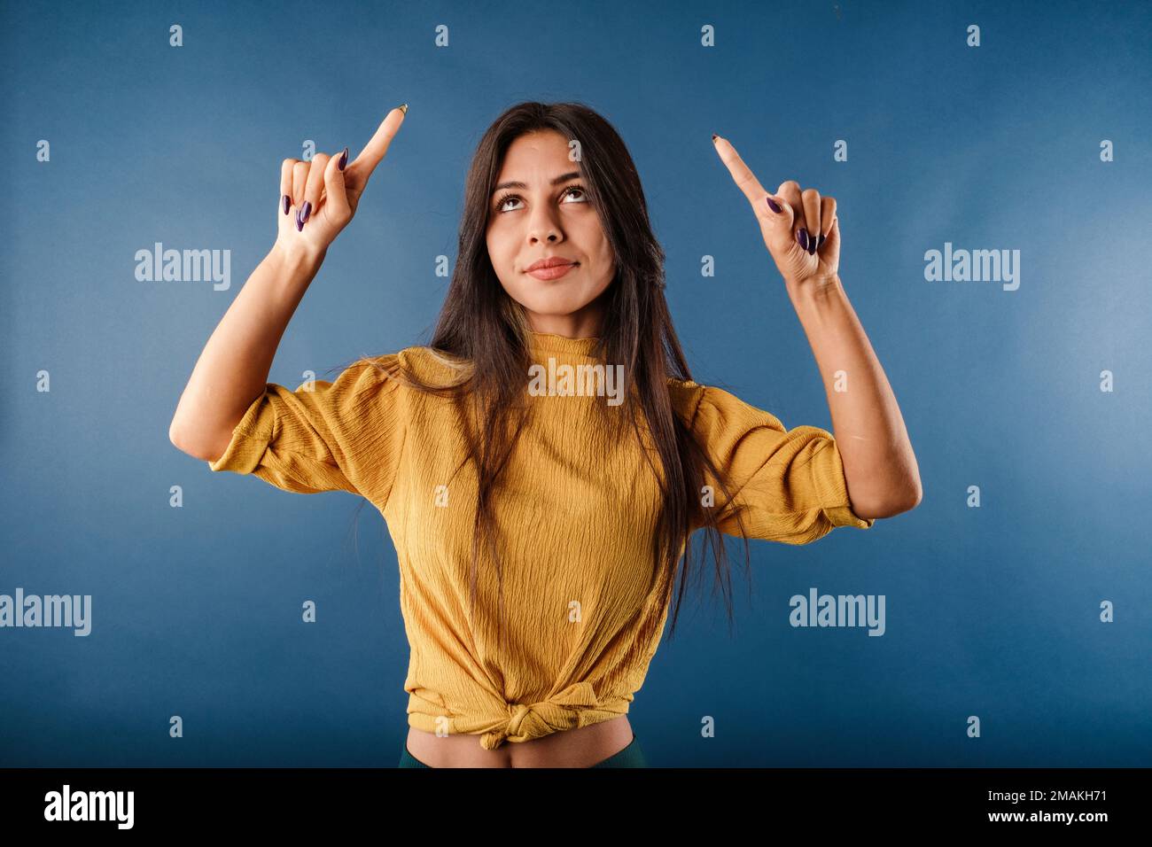Young beautiful woman wearing yellow top isolated over blue background ...